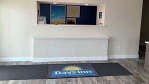 Uma área de recepção com balcão, um painel fixado na parede e um tapete com o logotipo Days Inn.