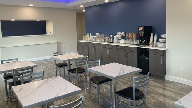Uma cozinha moderna com bancadas de mármore, uma área de café embutida e um espaço de estar com cadeiras e mesas de metal.