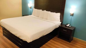 Quarto de hotel com uma cama grande, mesa de cabeceira com telefone e luminárias fixadas na parede.