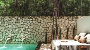 Paredes de pedra, uma piscina, uma cama com cobertura branca e um banquinho de madeira.