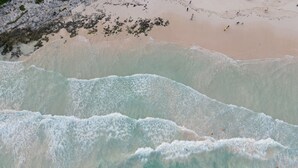 Vista aérea de uma praia com águas turquesa cristalinas e uma costa arenosa.