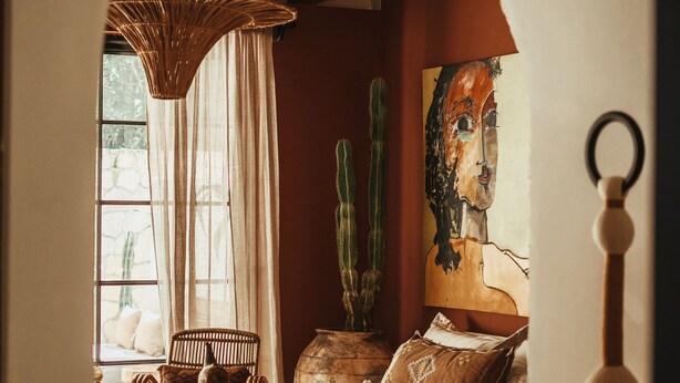 Uma sala de estar aconchegante com um sofá, uma mesa de centro e uma poltrona. Há um quadro na parede e uma janela com cortinas.