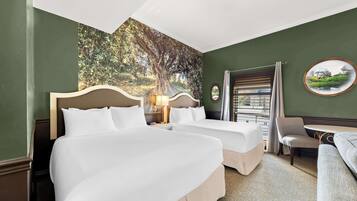 Quarto de hotel com duas camas, um sofá, uma mesinha e vista para uma árvore pela janela.