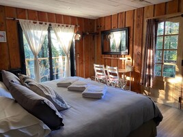 Quarto com painéis de madeira, uma cama, cadeiras e uma televisão.