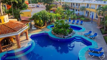 Uma área de piscina com várias piscinas, espreguiçadeiras e vegetação ao redor.