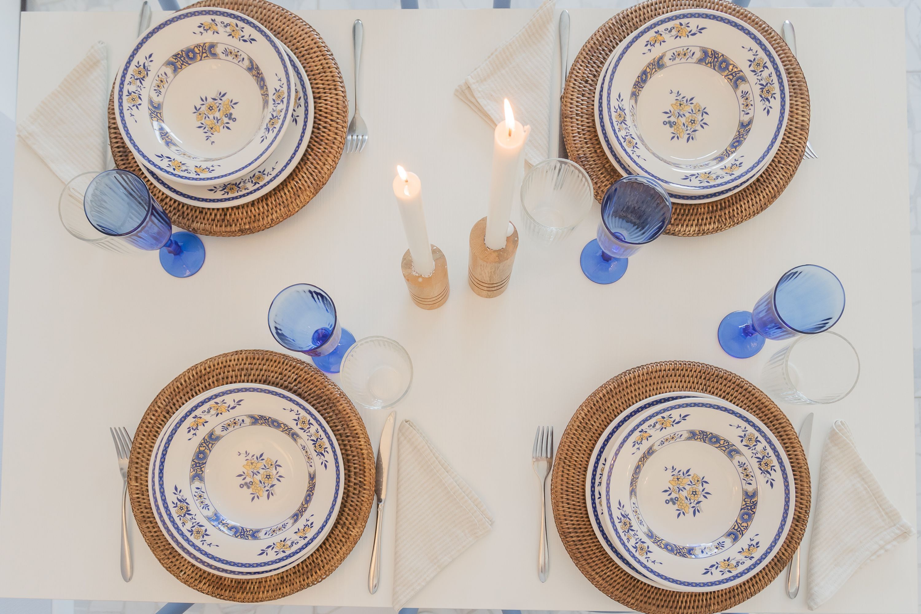 Uma mesa posta com pratos florais em azul e branco, talheres e copos de vidro azul.