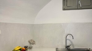 Uma cozinha com bancada branca, pia de aço inoxidável e armários cinzentos.