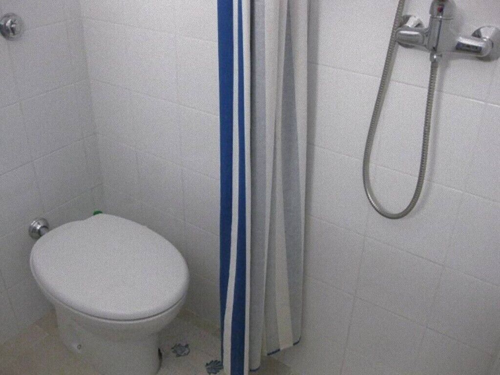 Um banheiro pequeno e branco com vaso sanitário, chuveiro e torneira fixada na parede.