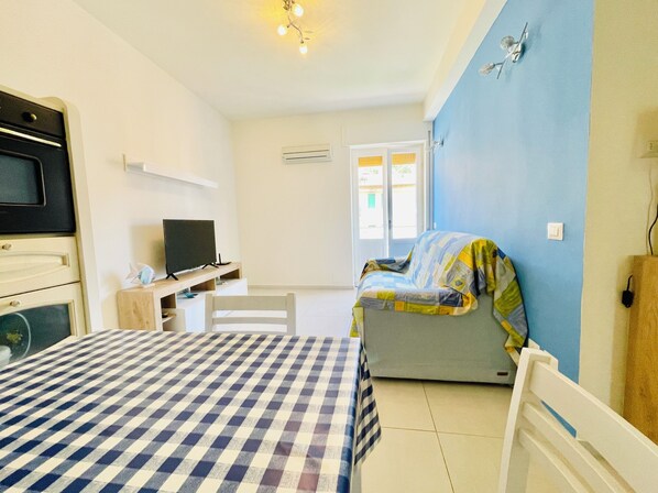 Um quarto com cama, televisão em um suporte, sofá e janela.