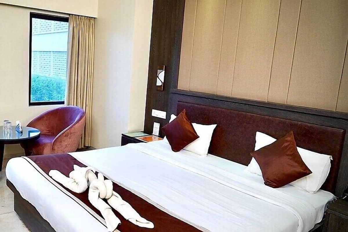 Quarto de hotel com cama, duas poltronas, uma mesa pequena e uma janela com cortinas.