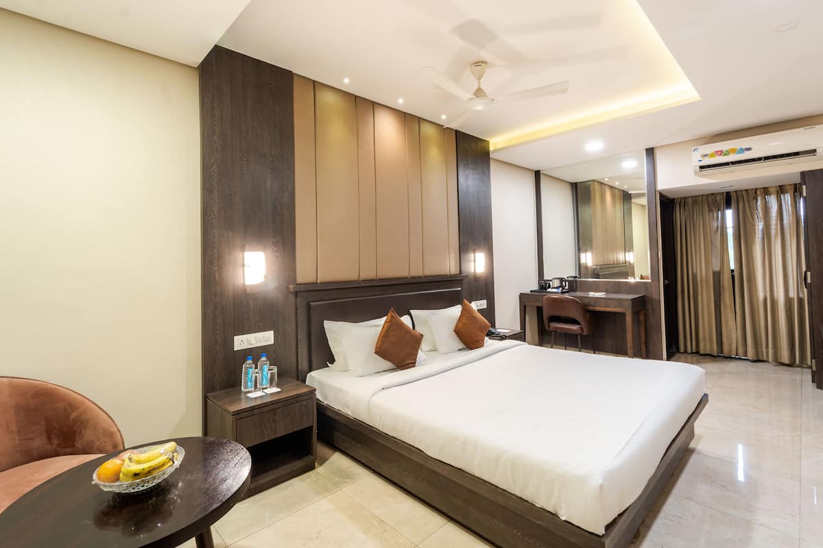 Quarto de hotel com cama grande, escrivaninha, cadeira, mesinha com frutas e ventoinha no teto.