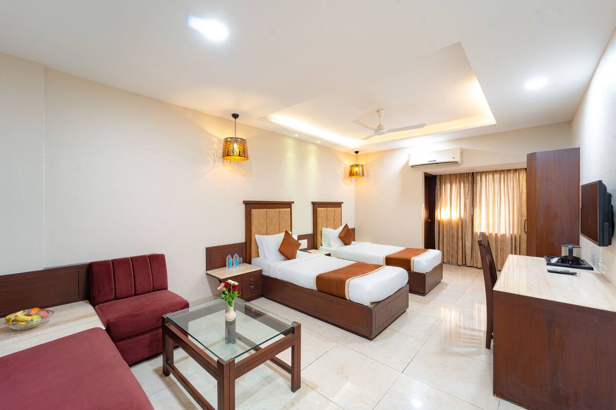 Quarto de hotel com duas camas, um sofá, uma mesa de vidro e uma televisão.