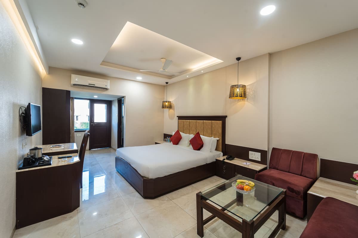 Quarto de hotel com cama, escrivaninha, cadeira, mesa de vidro e sofá.