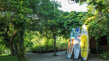 Uma passarela pavimentada bordeada por árvores e três pranchas de surf encostadas em uma parede.