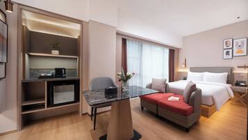 Quarto de hotel moderno com cama, sofá, mesa de jantar e cozinha compacta.
