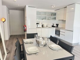Uma cozinha moderna com armários brancos, uma mesa de jantar posta com pratos e copos, e um extintor de incêndio na parede.