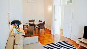 Uma sala de estar moderna com sofá, uma mesa de jantar com cadeiras, um aparador para TV e um tapete listrado em preto e branco.