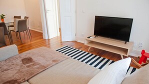 Uma sala de estar moderna com sofá, televisão em um suporte de madeira, área de refeições com cadeiras e um tapete listrado.