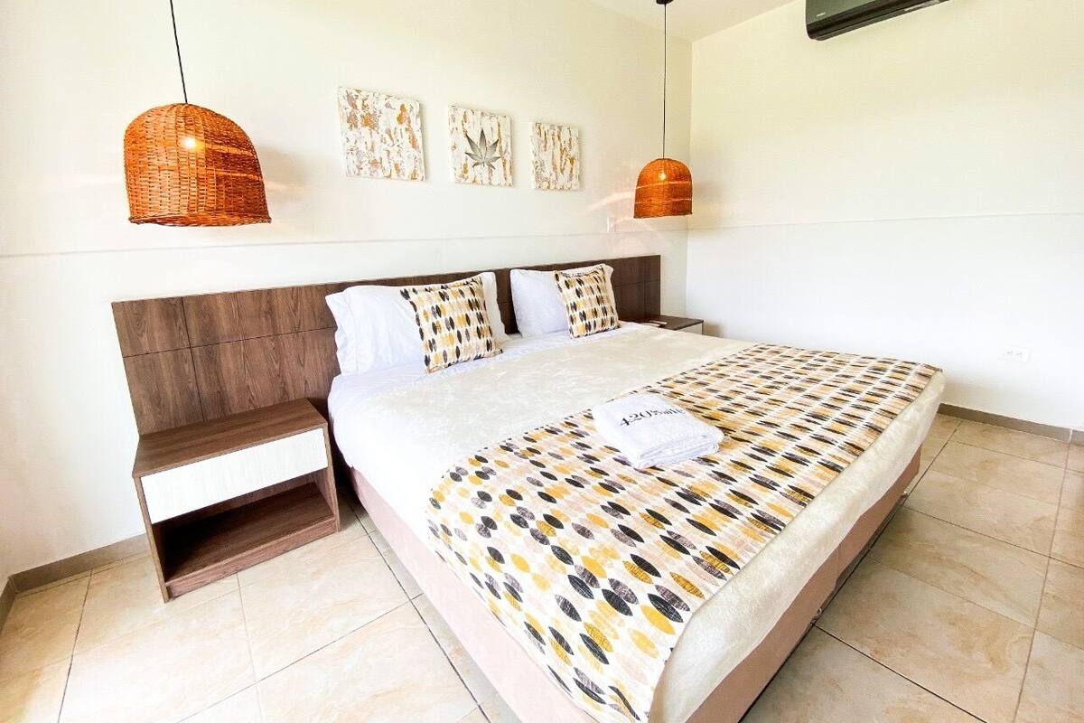 Quarto com cama, mesas de cabeceira, cabeceira, obras de arte na parede e luminárias pendentes.