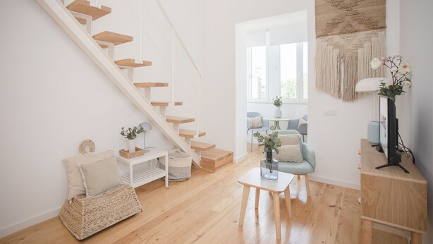 Uma sala de estar moderna com escada de madeira, uma mesa pequena com um vaso e uma cadeira.