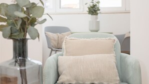 Um quarto com uma poltrona azul clara, uma mesa pequena e um vaso com folhagem verde.