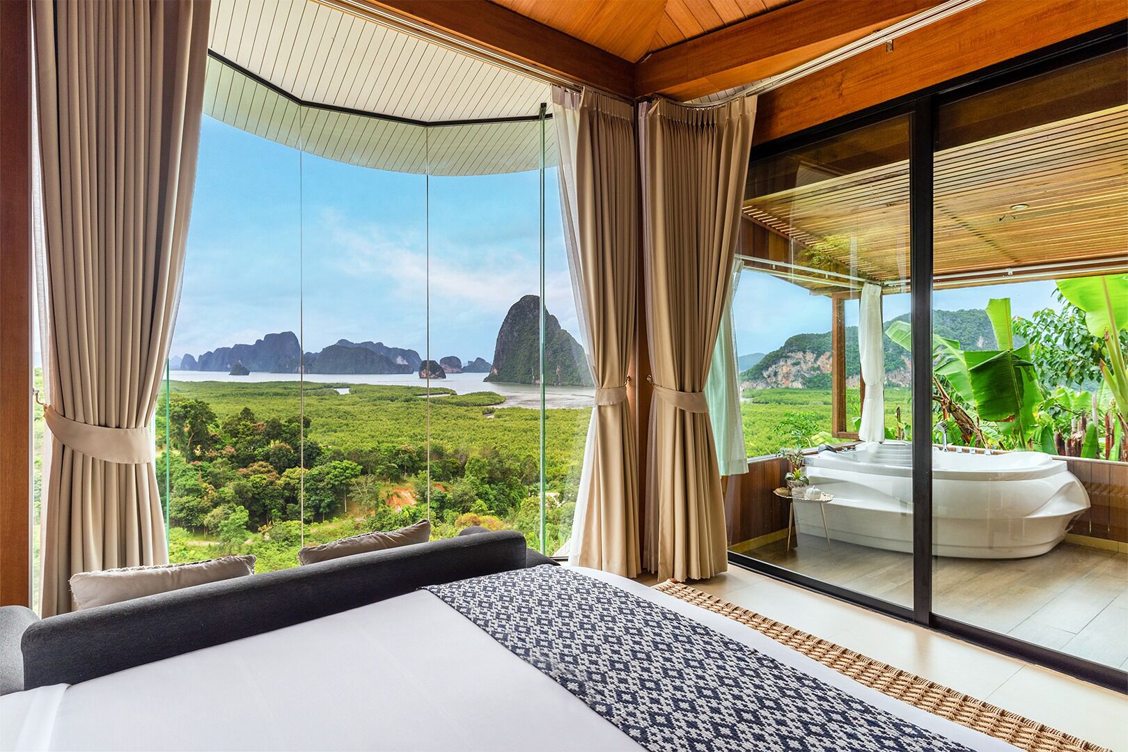 Quarto com uma cama grande, vista para uma banheira de hidromassagem e paisagem exuberante lá fora.