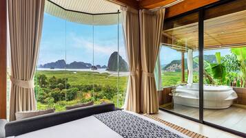 Quarto com uma cama grande, vista para uma banheira de hidromassagem e paisagem exuberante lá fora.