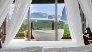 Quarto com uma cama grande, uma banheira branca e vista para uma paisagem montanhosa.