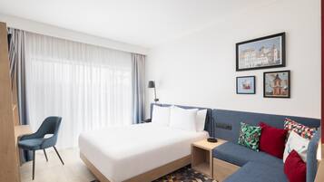 Quarto de hotel com uma cama, escrivaninha, cadeira, sofá e mesa de cabeceira. Três quadros emoldurados na parede.