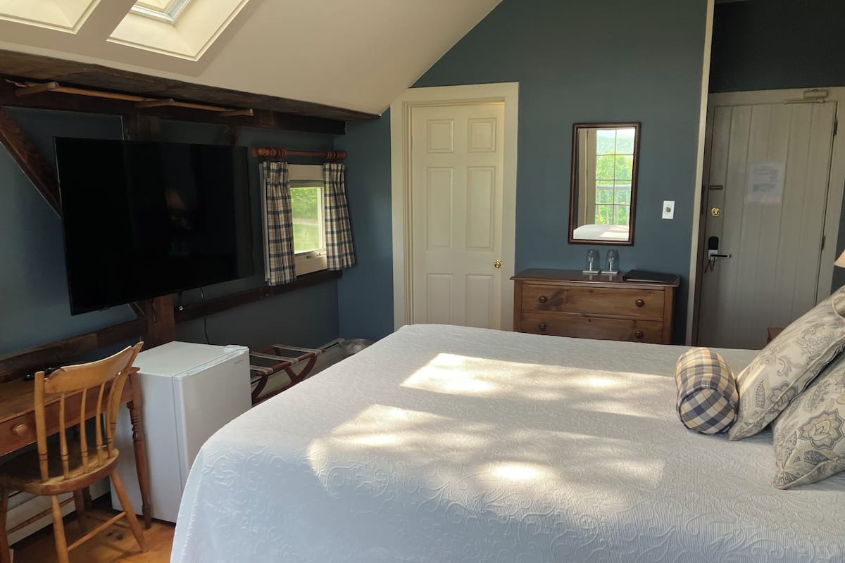 Quarto com cama, escrivaninha, televisão e cómoda.