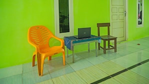 Quarto com parede verde, janela, porta, mesa com um laptop e duas cadeiras.