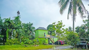 Um edifício verde com varanda, rodeado por vegetação exuberante e palmeiras.