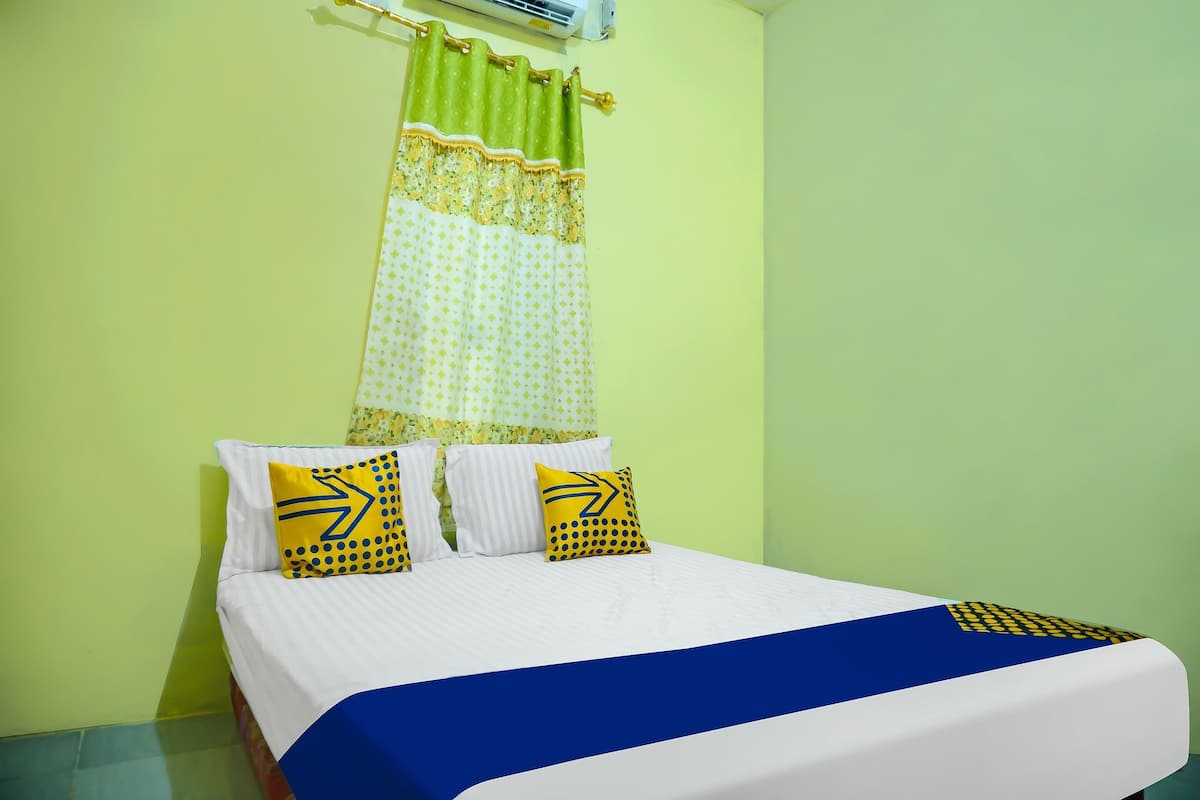 Cama com roupa de cama branca e detalhes azuis, cortina verde e almofadas amarelas com padrões pretos.