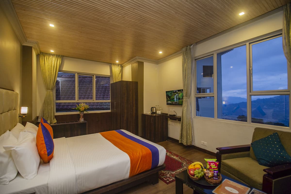 Quarto de hotel com cama, secretária, televisão e vista para as montanhas.