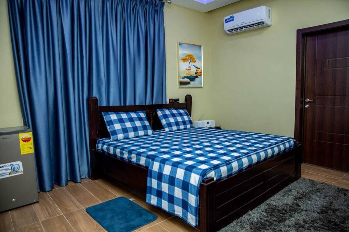 Quarto com colcha xadrez, cortina azul, pintura na parede e ar condicionado.
