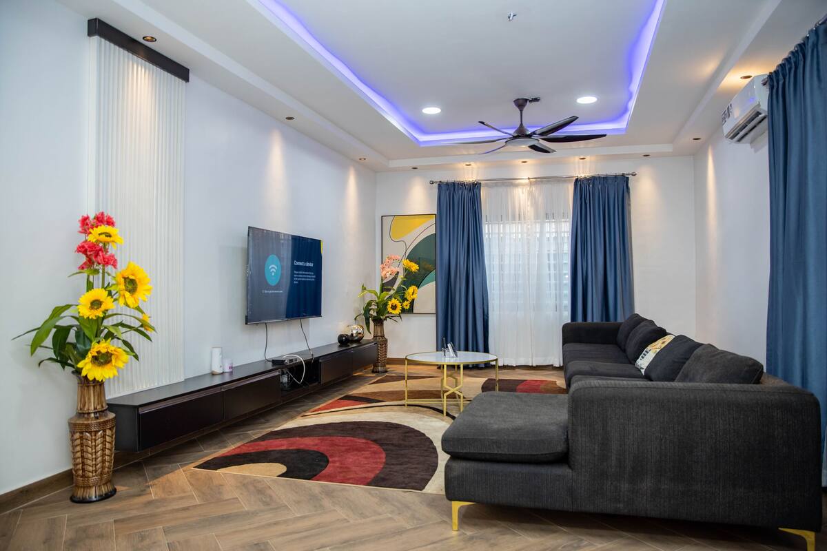 Uma sala de estar moderna com sofá, televisão e plantas decorativas.