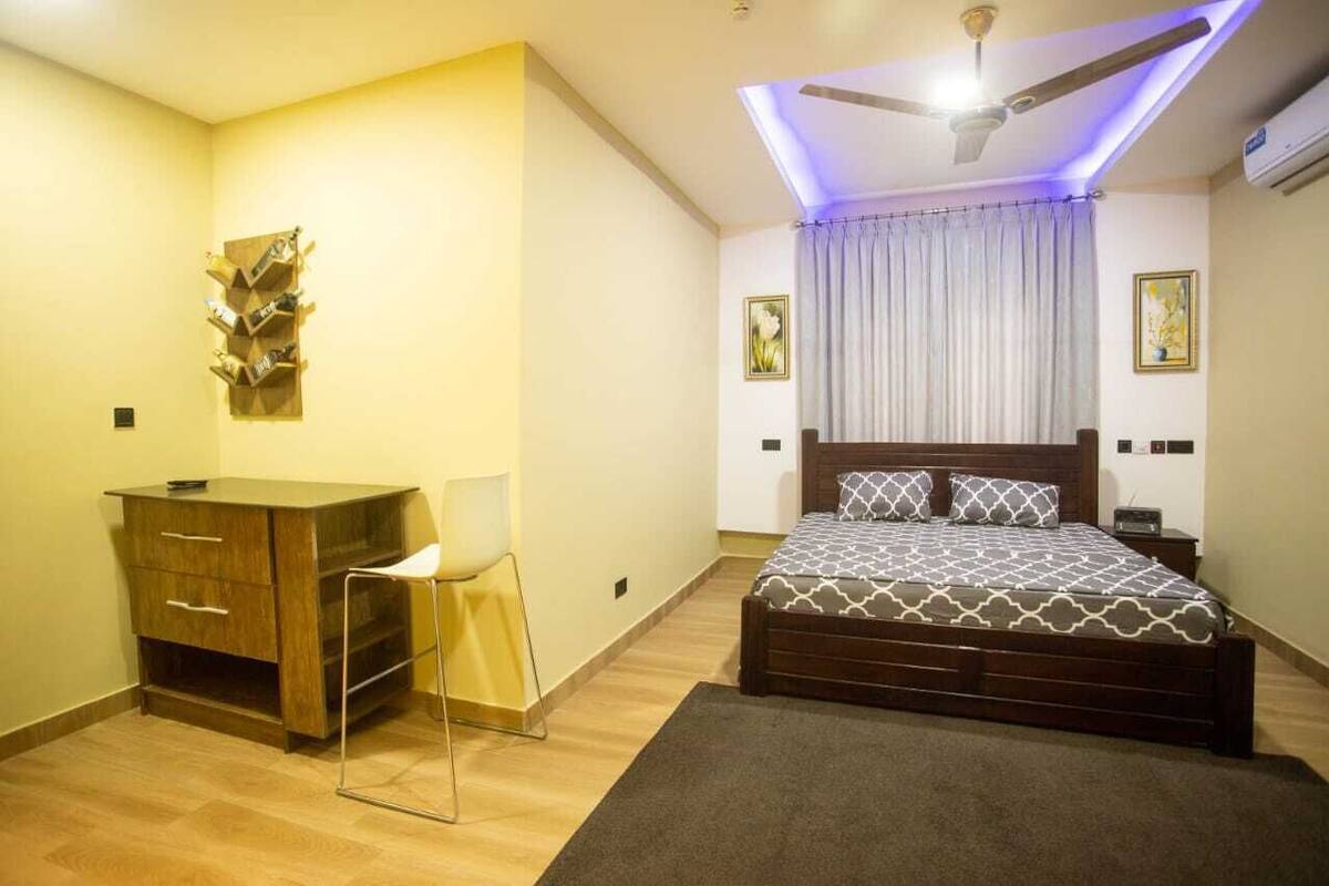 Quarto com cama, escrivaninha, cadeira e ventilador de teto.