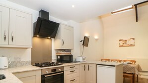Cozinha compacta com forno Bosch, micro-ondas e torradeira. Possui área de refeições com mesa e cadeiras.