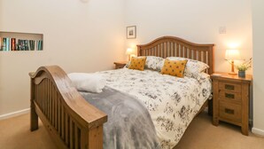 Quarto com cama de madeira, duas mesas de cabeceira com abajures, uma estante e um lustre.