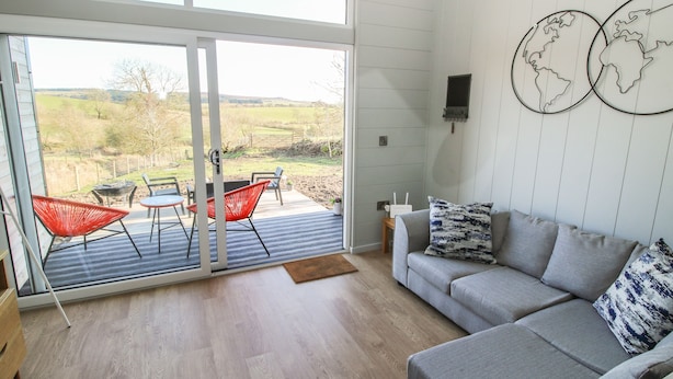 Uma sala de estar moderna com um sofá cinzento, uma cadeira vermelha e vista para um jardim através de portas de vidro.