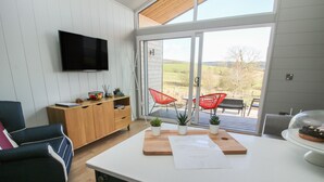 Cozinha moderna com armário de madeira, televisão de tela plana e área de jantar com cadeiras vermelhas.