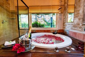 Um banheiro luxuoso com uma banheira grande, uma garrafa de champanhe e pétalas de rosas.