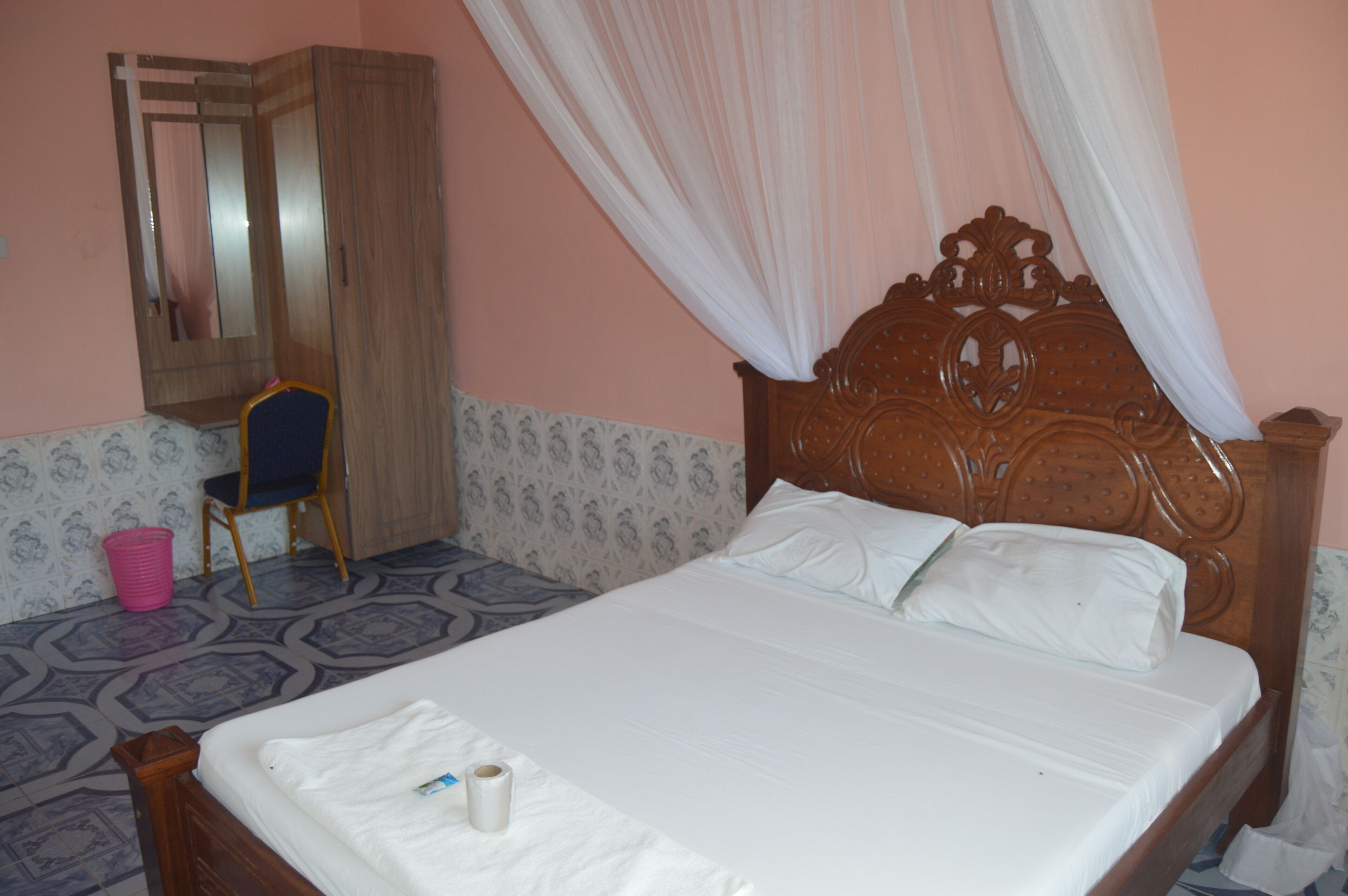 Quarto com cama de madeira, uma cadeira, guarda-roupa e espelho.