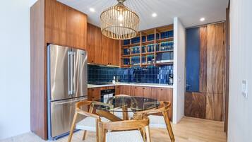 Cozinha moderna com armários de madeira, geladeira de aço inoxidável, mesa de jantar de vidro e painel de azulejos azuis.