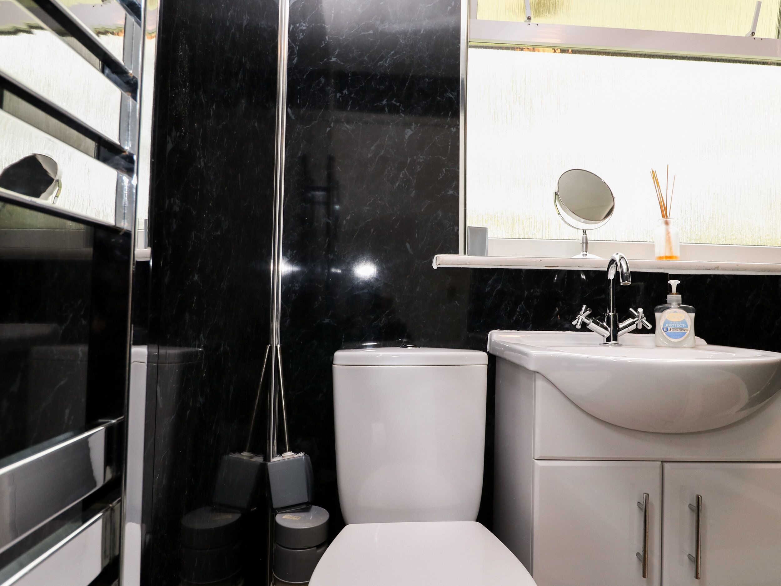 Uma casa de banho moderna com uma pia de mármore preto, sanita e chuveiro.