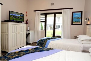 Quarto de hotel com duas camas, televisão, escrivaninha e janela com cortinas.