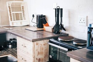 Uma cozinha com fogão embutido, um ventilador branco e um conjunto de utensílios pretos sobre o balcão.
