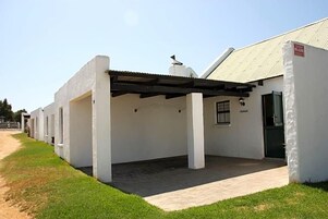 Um edifício branco com área externa coberta, uma porta com a inscrição 'Hôtel' e céu claro.