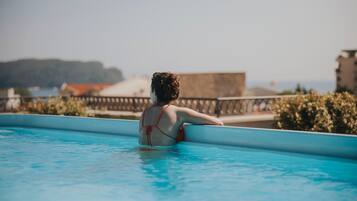 Uma pessoa relaxando em uma piscina com vista para prédios e colinas ao fundo.