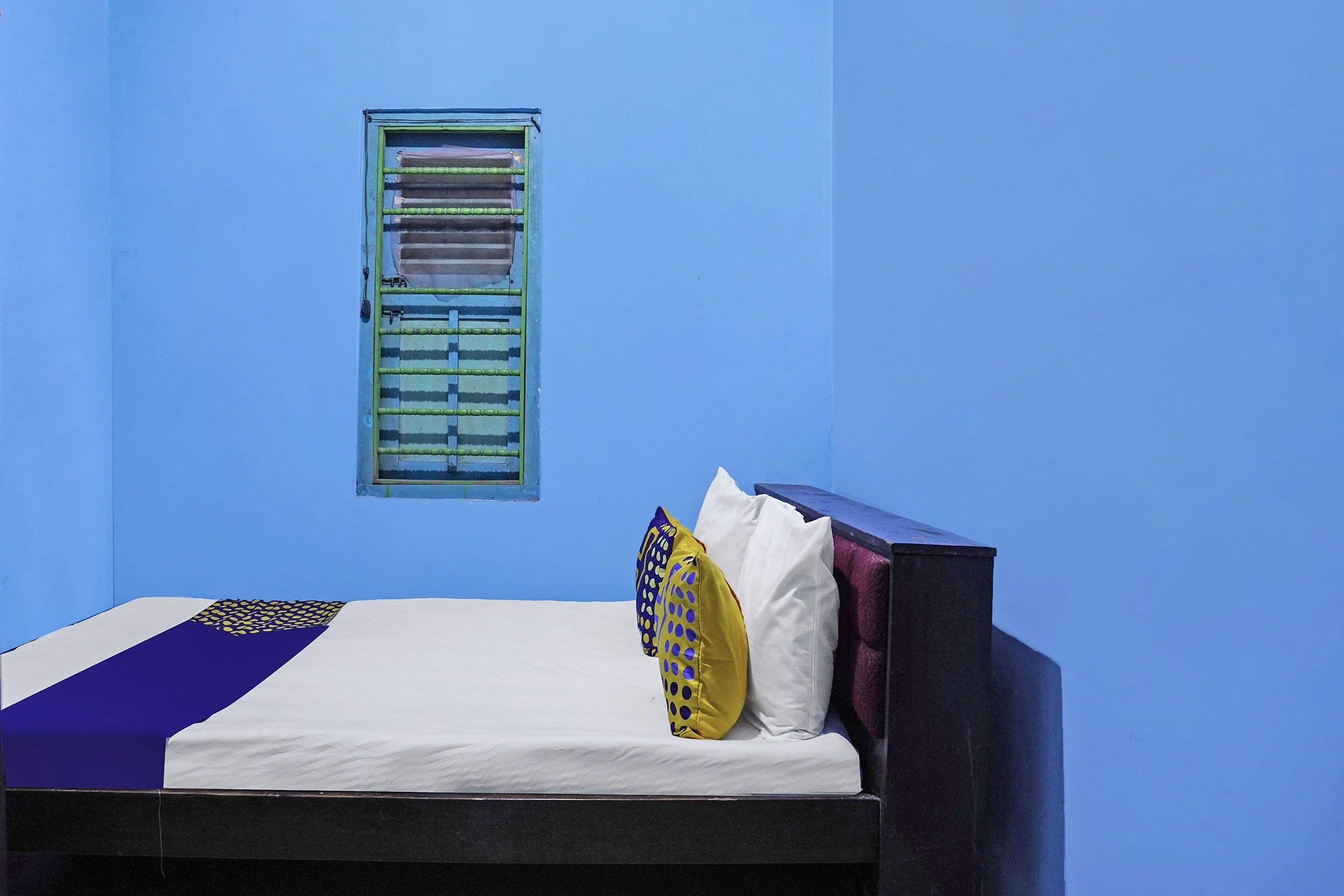 Um quarto com uma cama de solteiro, uma janela com persiana azul e uma parede lisa.